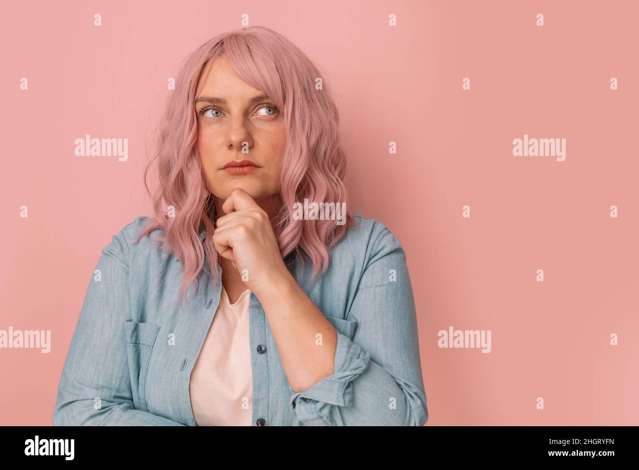 Focused young woman feeling thoughtful keeps hand near mouth looks up ...