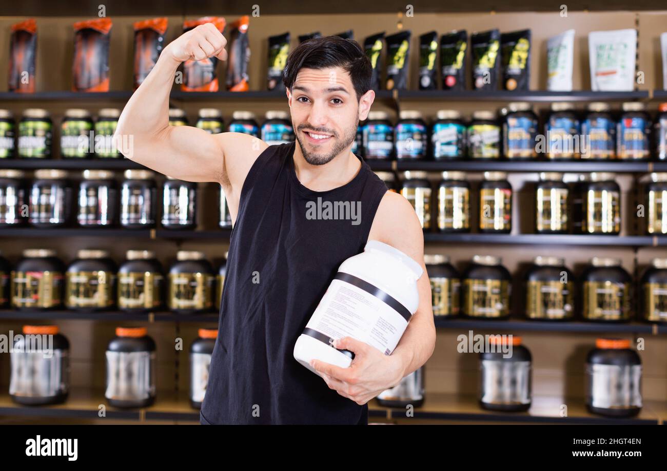 Young bodybuilder showing his biceps and holding pot of sport nutrition ...
