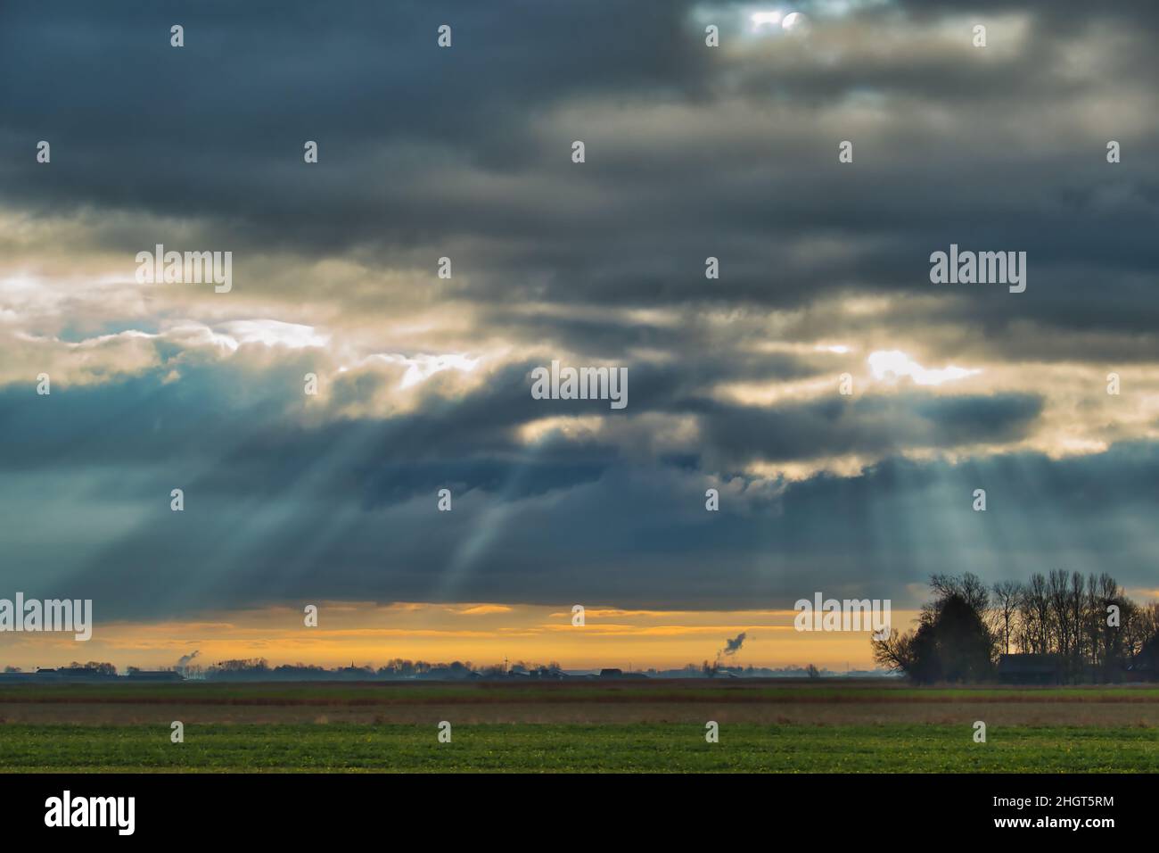Sun rays through dark clouds above a Dutch farm. Farm and fields in the ...