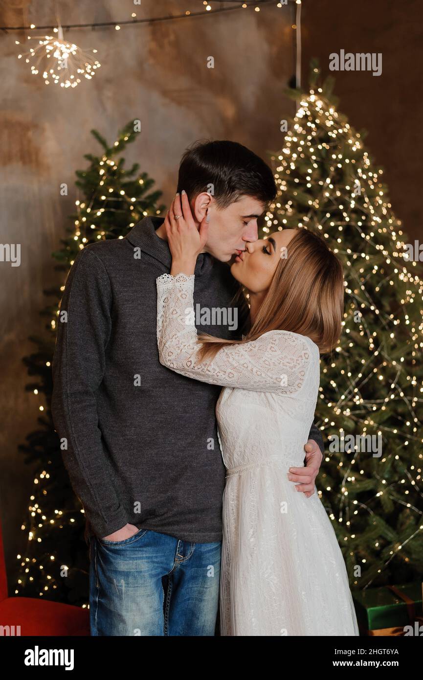 A guy and a girl hug and kiss against the background of a Christmas tree and a red sofa Stock ...