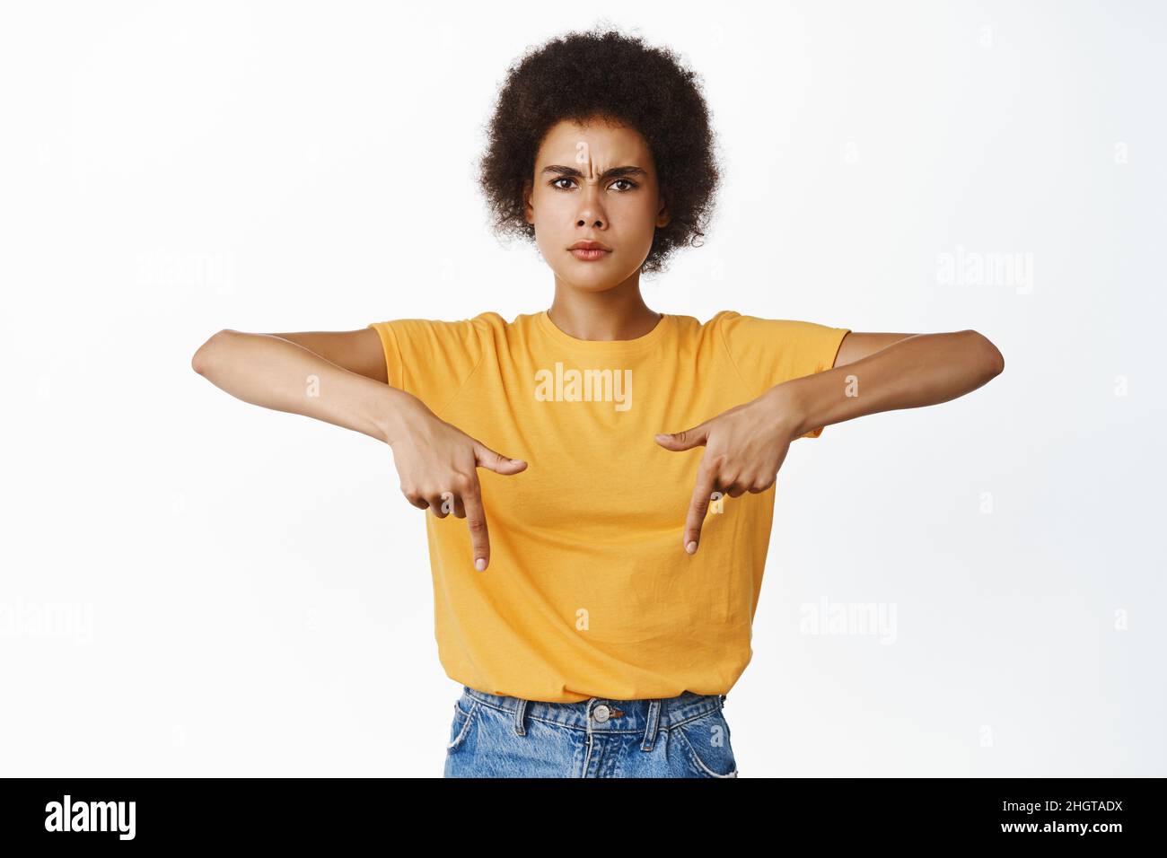 Confused and suspicious attractive female model, pointing fingers down ...