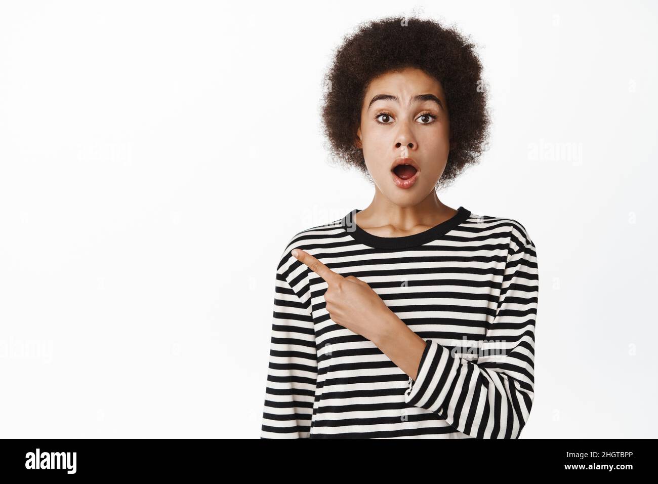 Portrait of black teen girl looking surprised, pointing finger left ...