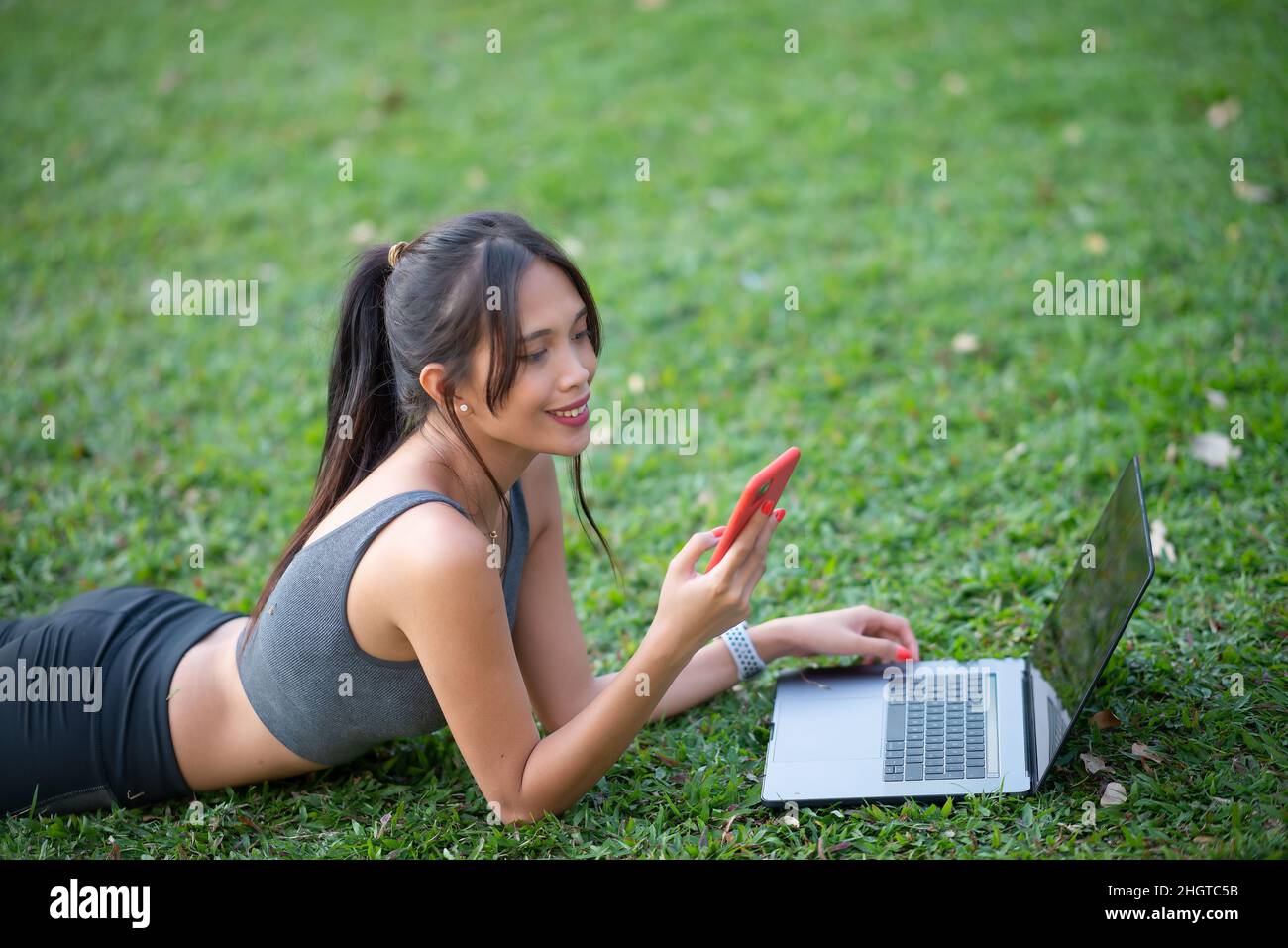 Young And Beautiful Asian Woman Lying On The Park Grass Using Laptop