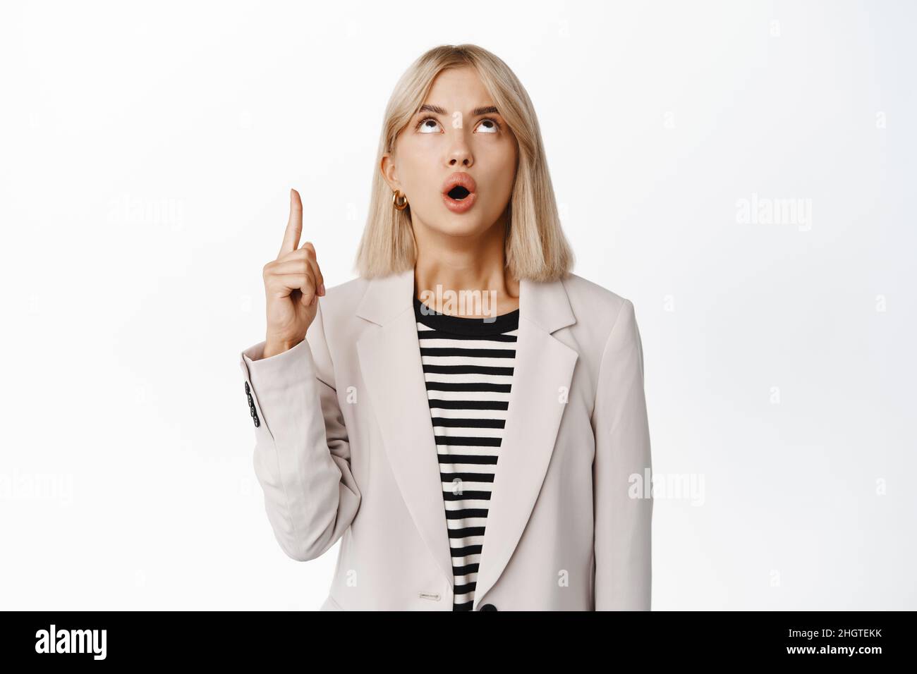Portrait of surprised blond woman in suit pointing, looking up with ...