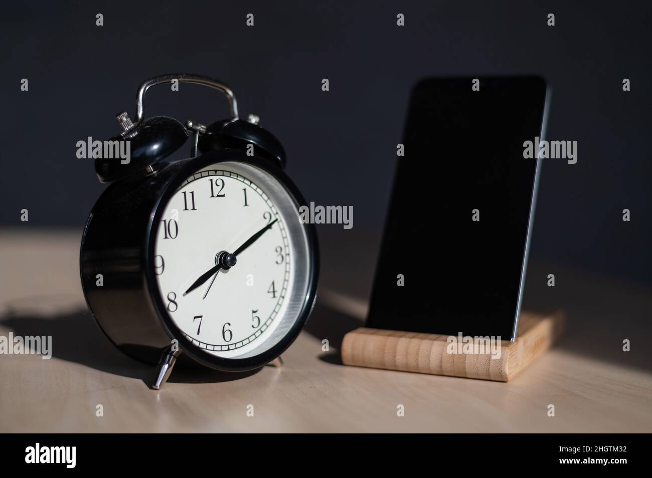 Classic alarm clock and smartphone on a stand on a wooden table. No ...