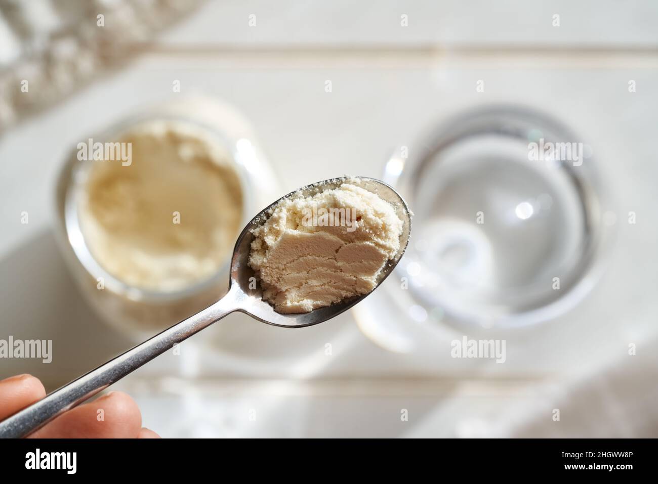 A spoonful of whey protein powder above a glass of water - preparation ...