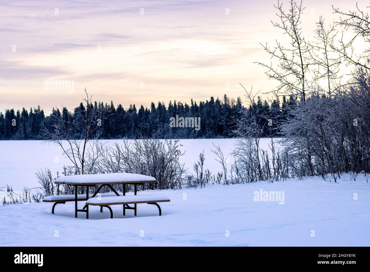 picnic table covered in snow on bank of frozen snow covered lake in ...