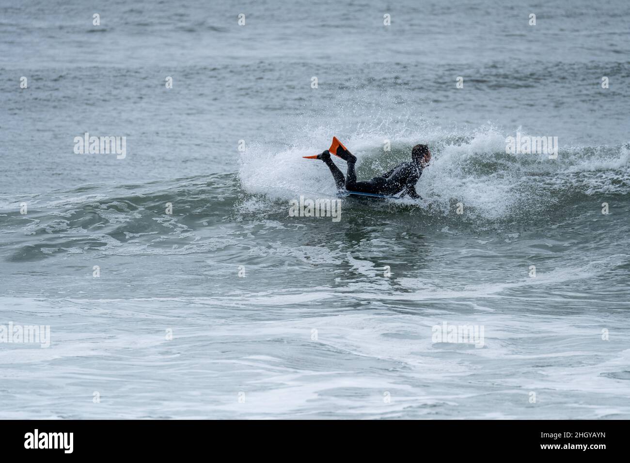 Bodyboarder performing a 360 trick surfing ocean wave on a cloudy ...