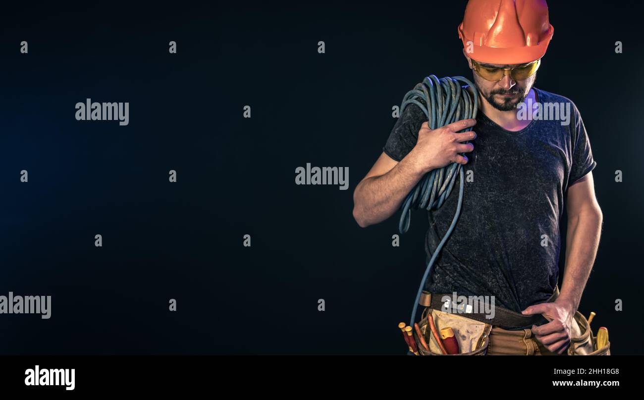 Male electrician with electric cable on a black background, copy space ...