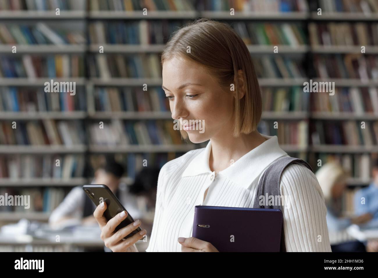Positive student girl using app on smartphone in college library Stock ...