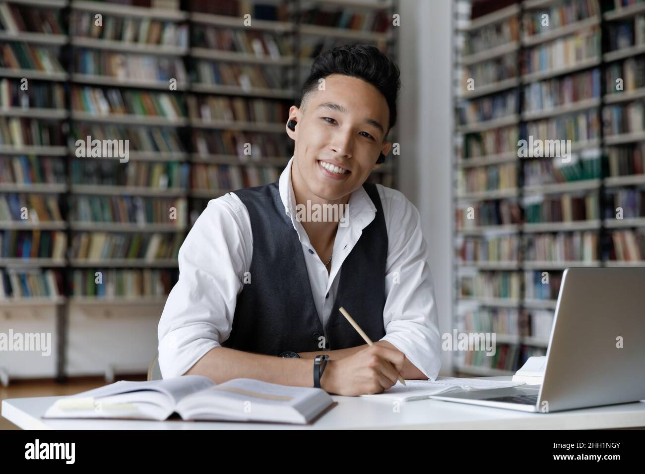 Happy Asian student with wireless earphones studying in library ...