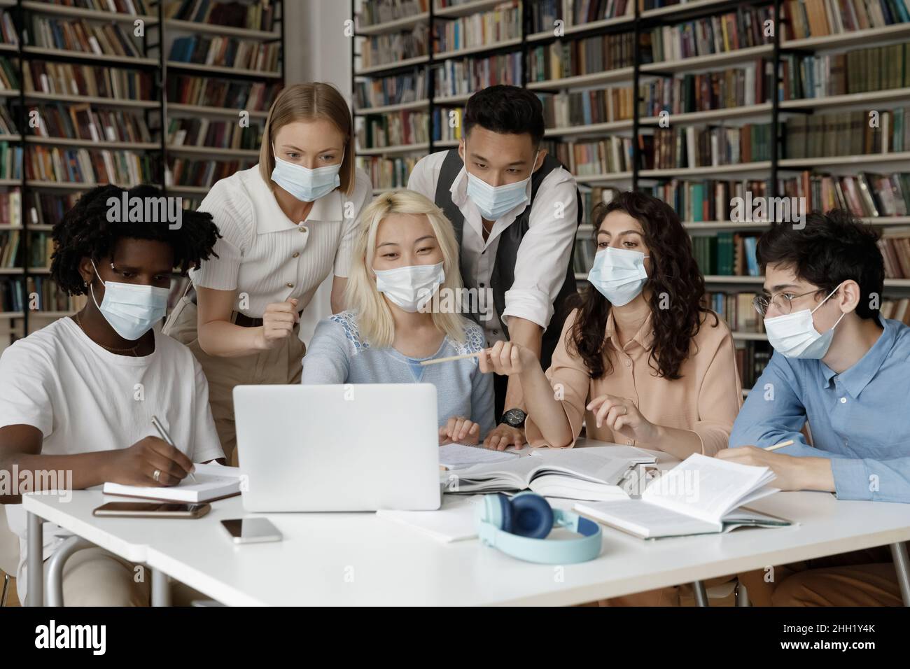 Interracial group of students wearing masks sitting at laptop Stock ...