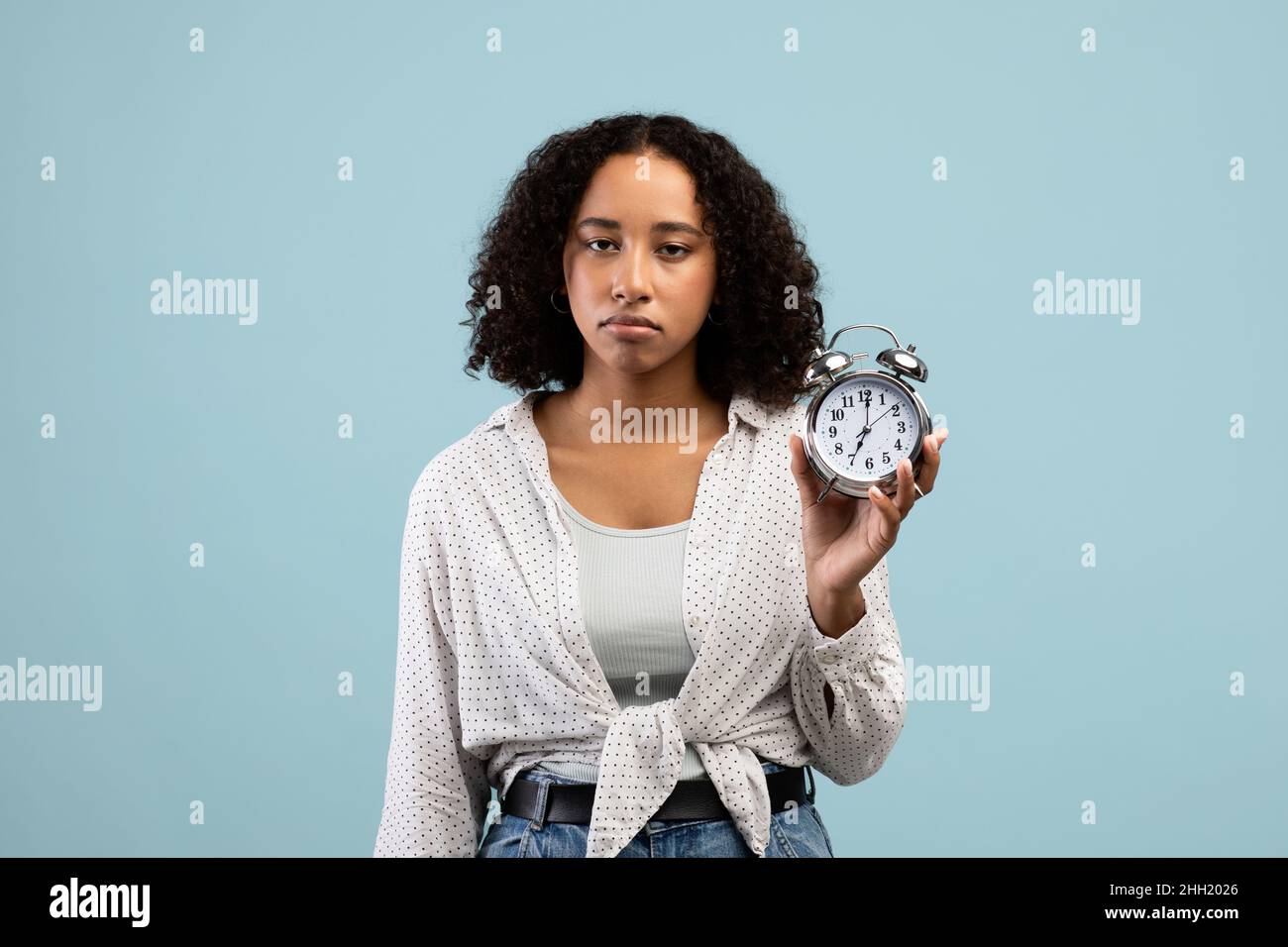 Bored young black female student showing alarm clock at camera over ...