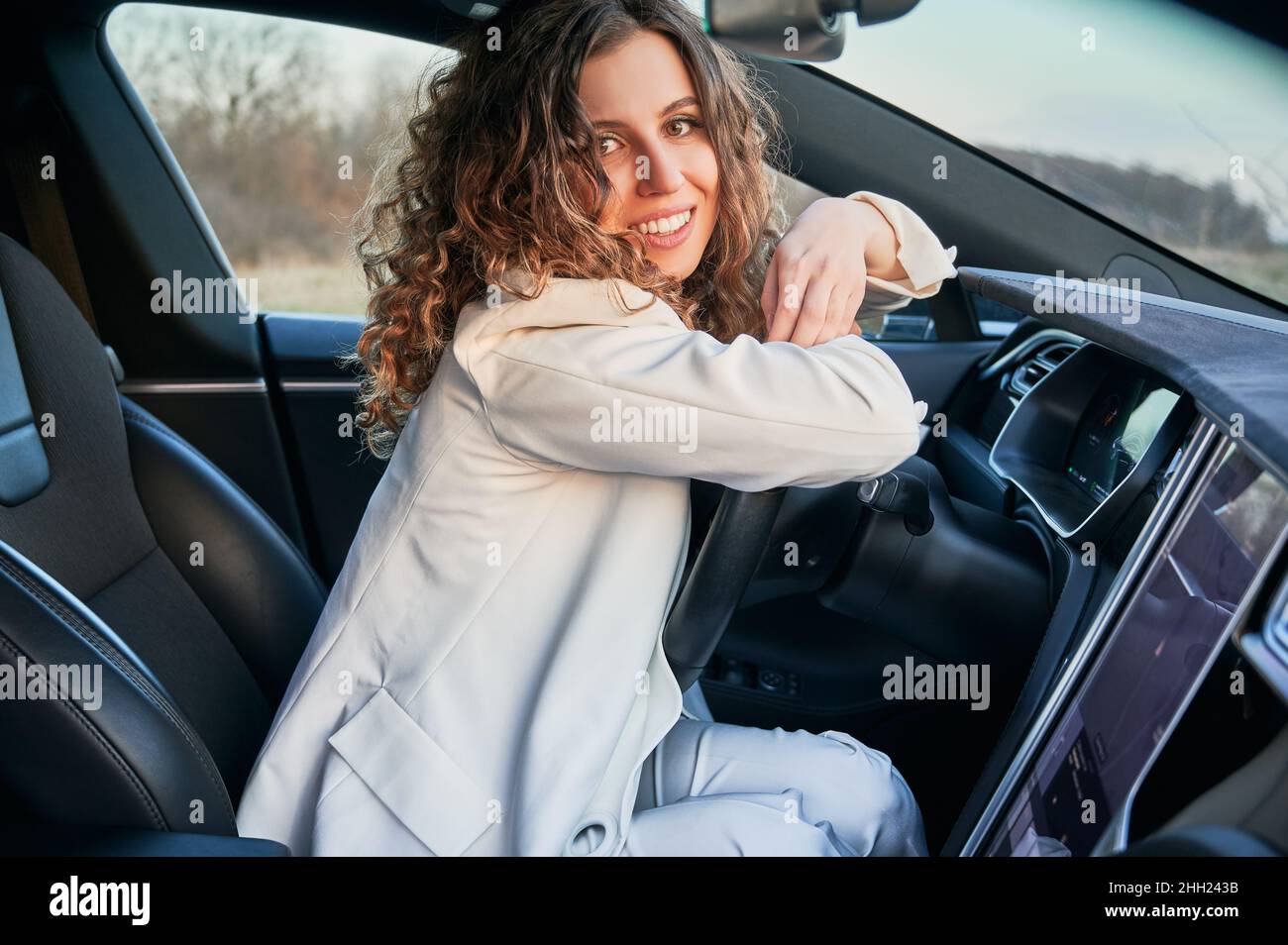 Portrait of beautiful curly lady inside electric car interior who ...