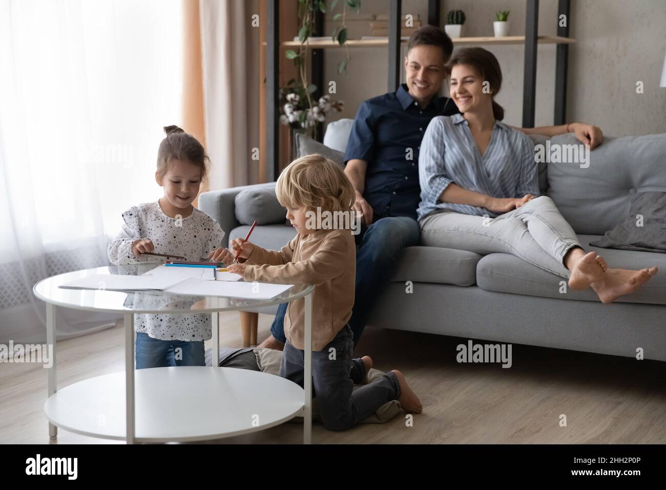 Happy millennial couple parents watching small kids drawing pictures ...