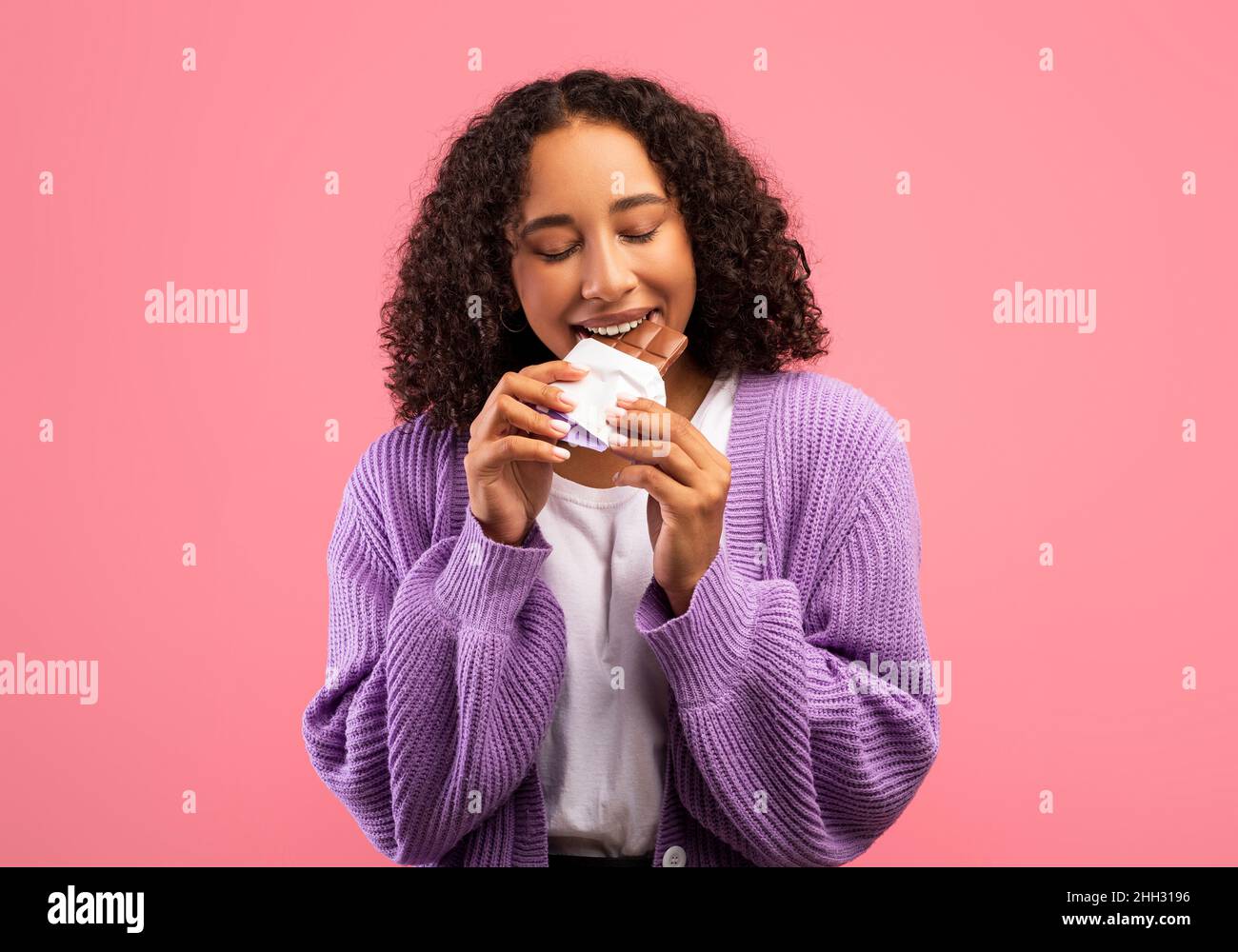 Beautiful young African American lady eating chocolate bar, enjoying ...