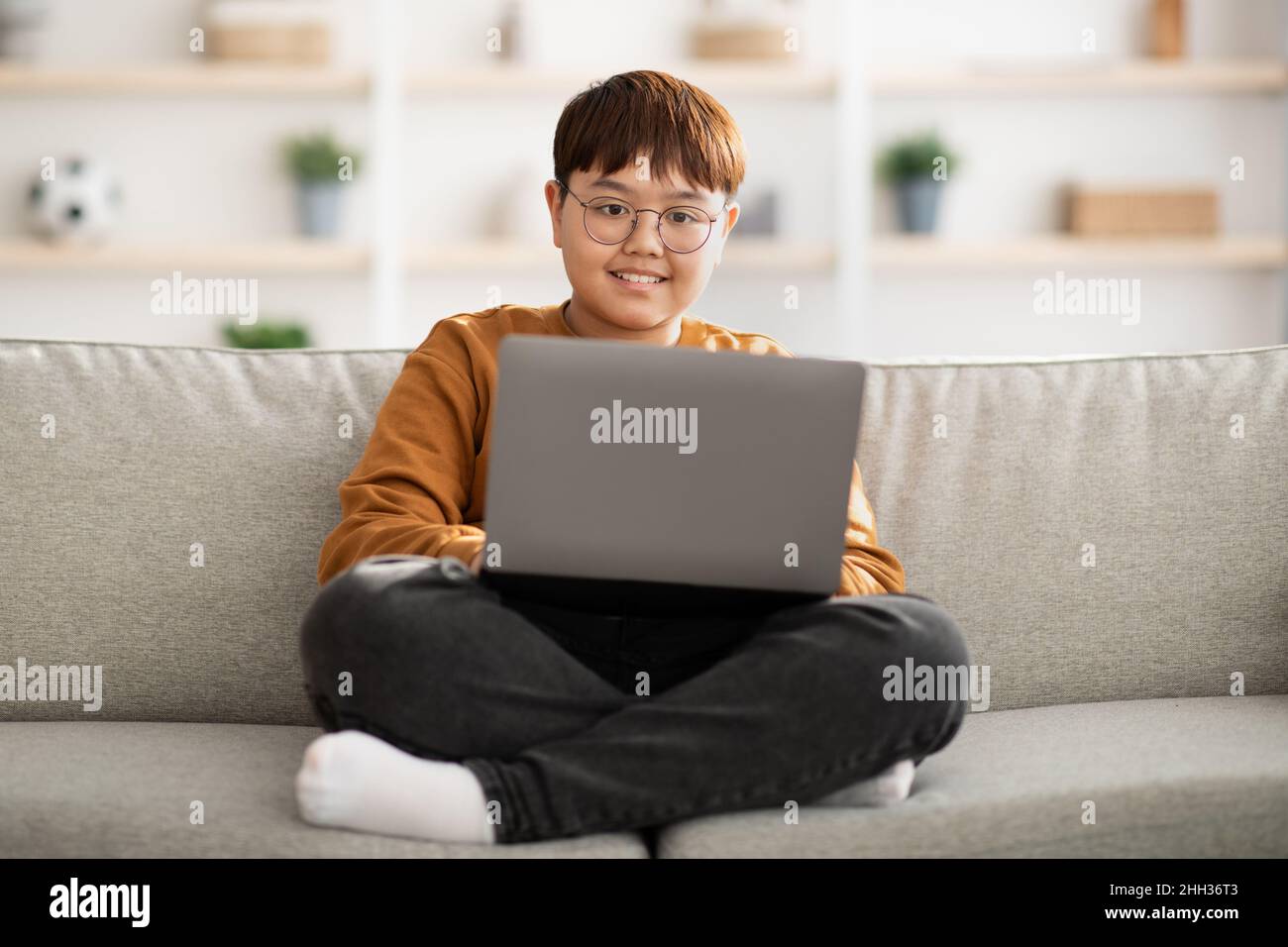 Happy chinese kid sitting on couch with laptop at home Stock Photo - Alamy