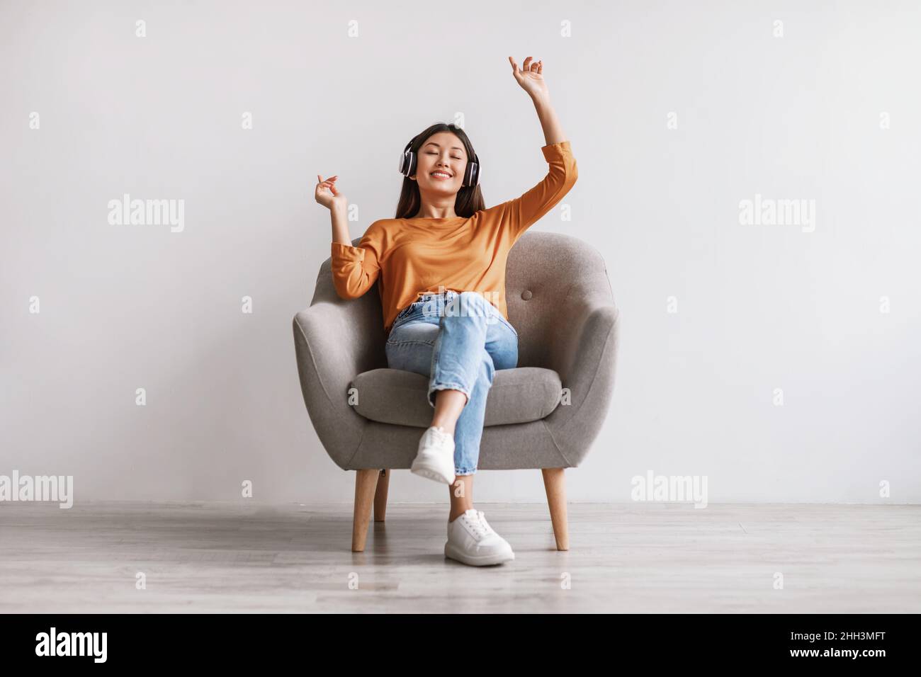 Full length of pretty young Asian woman listening to music in ...