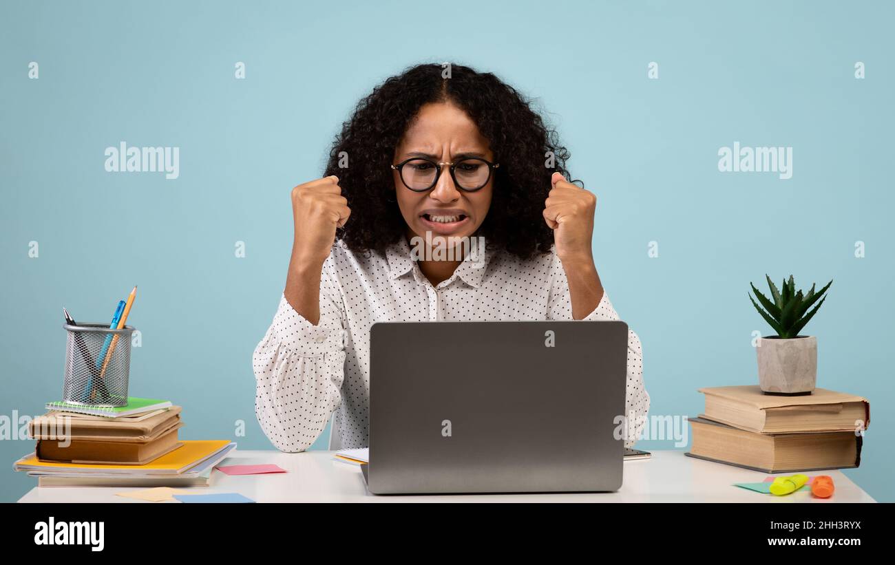 Young black woman in glasses sitting at desk, looking at laptop screen ...