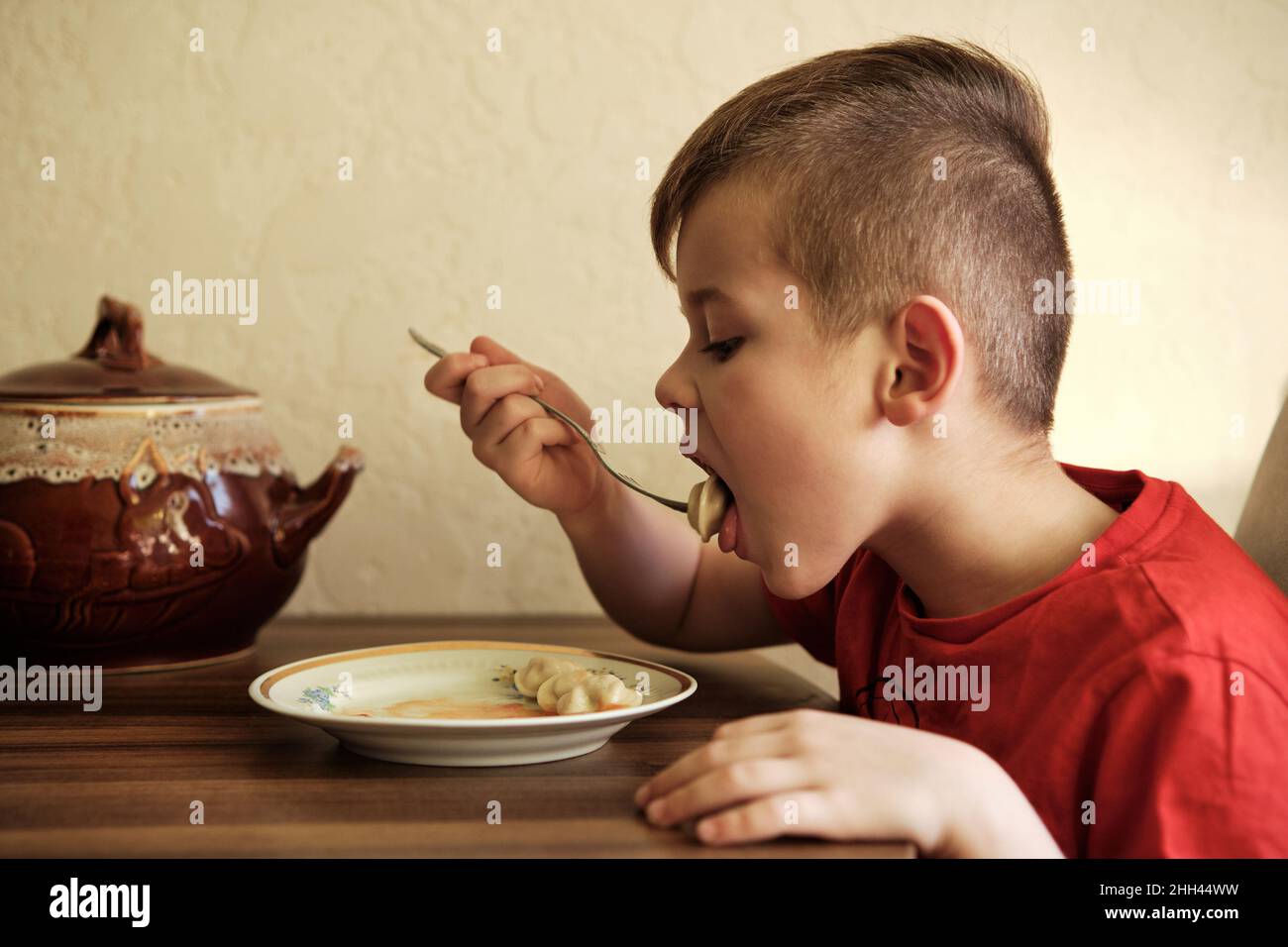 Cute Boy eating dumplings on the table in the kitchen. Hungry Child ...