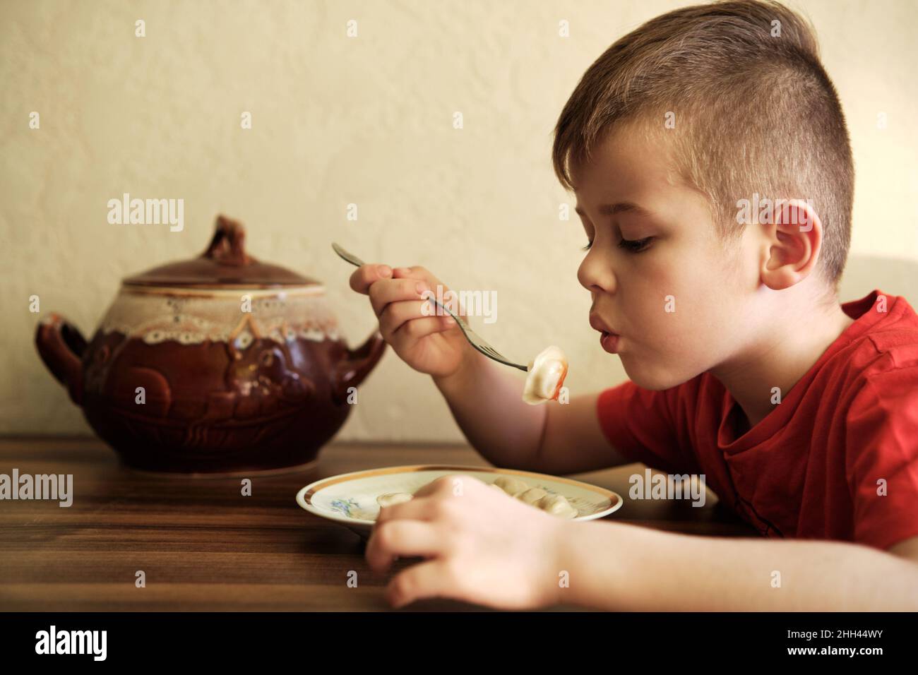 Cute Boy eating dumplings on the table in the kitchen. Hungry Child ...