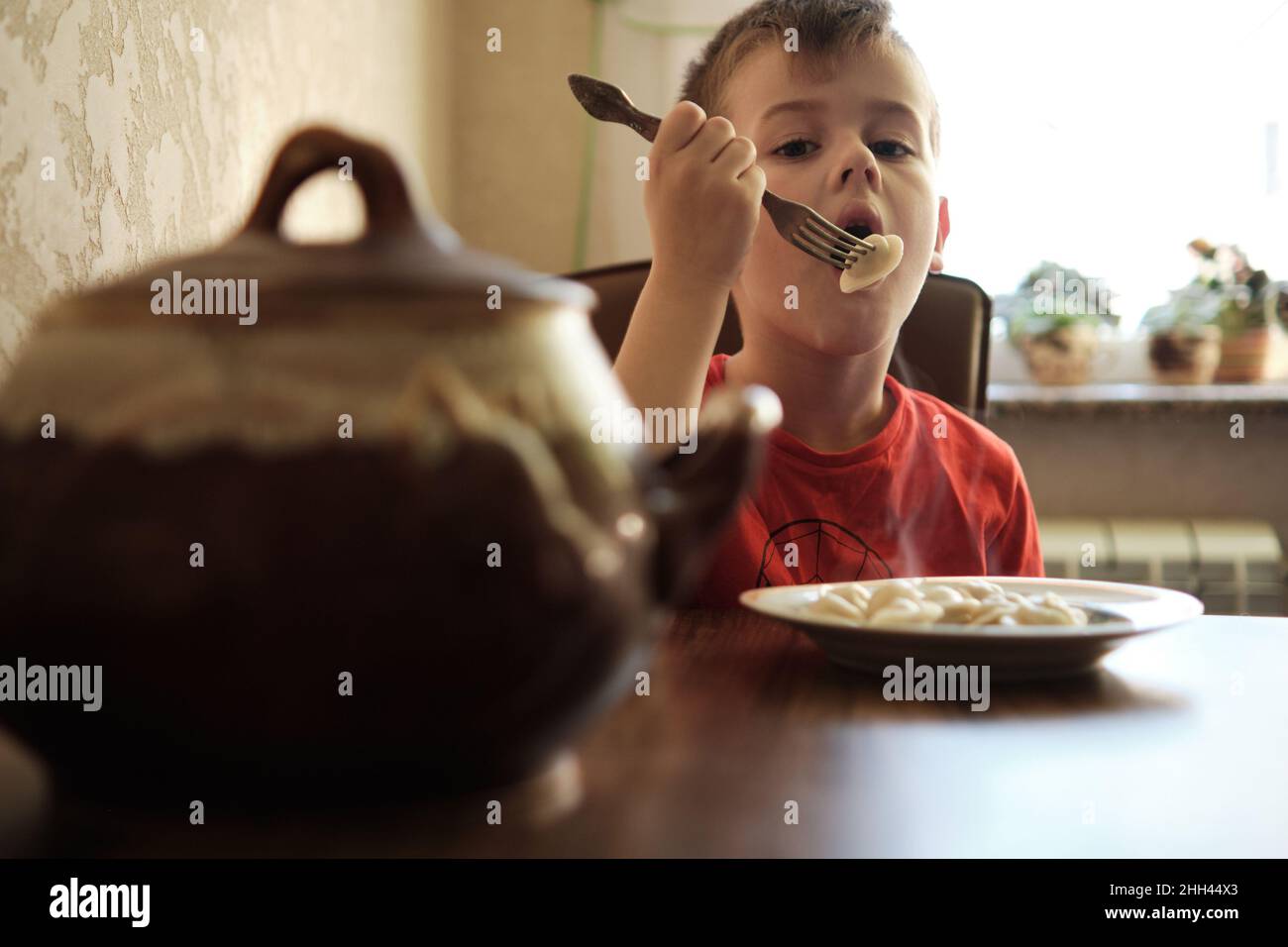 Cute Boy eating dumplings on the table in the kitchen. Hungry Child ...