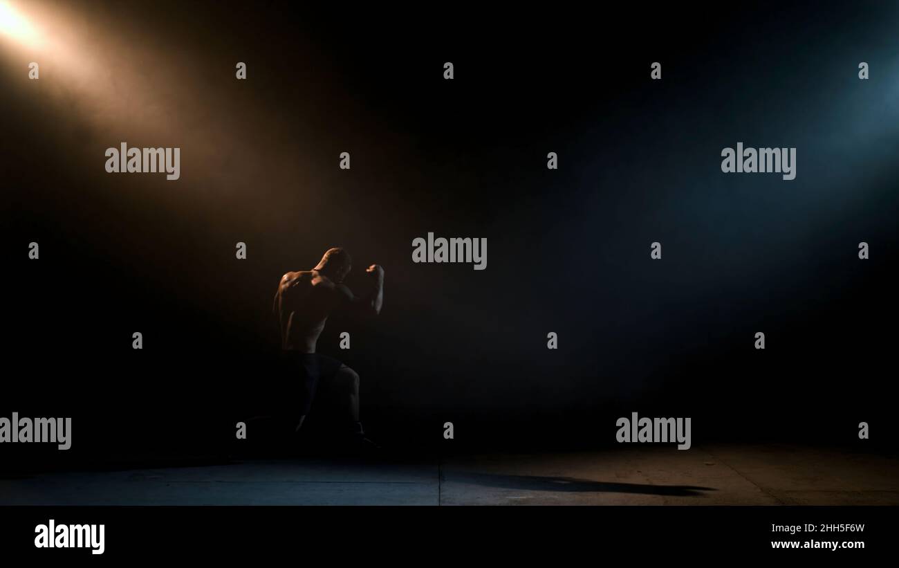 Boxer doing shadow Boxing in a dark room. Man of athletic build makes a ...