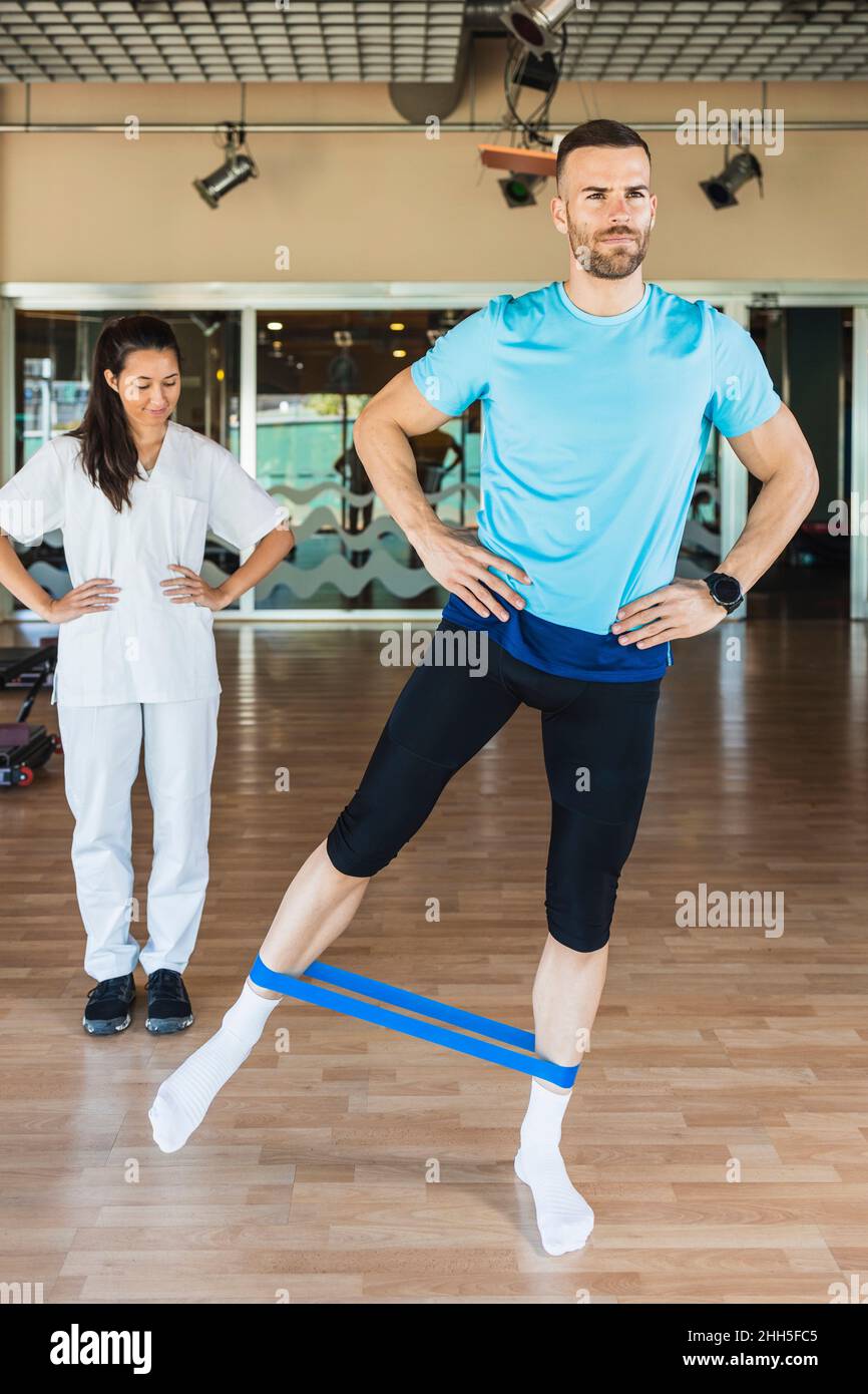 Sportsman with hands on hips exercising with resistance band in gym ...