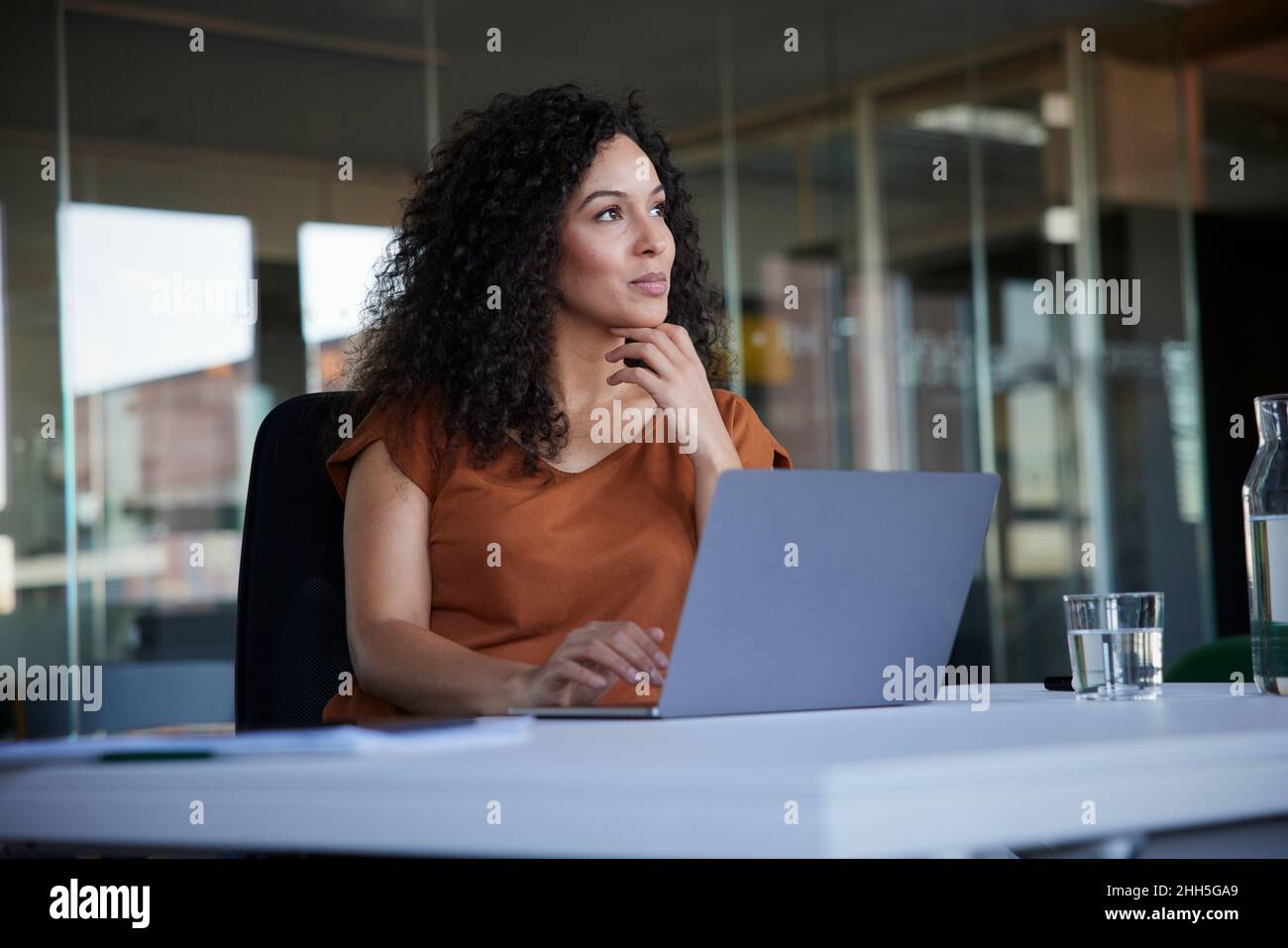 Smiling businesswoman with laptop contemplating at workplace Stock ...