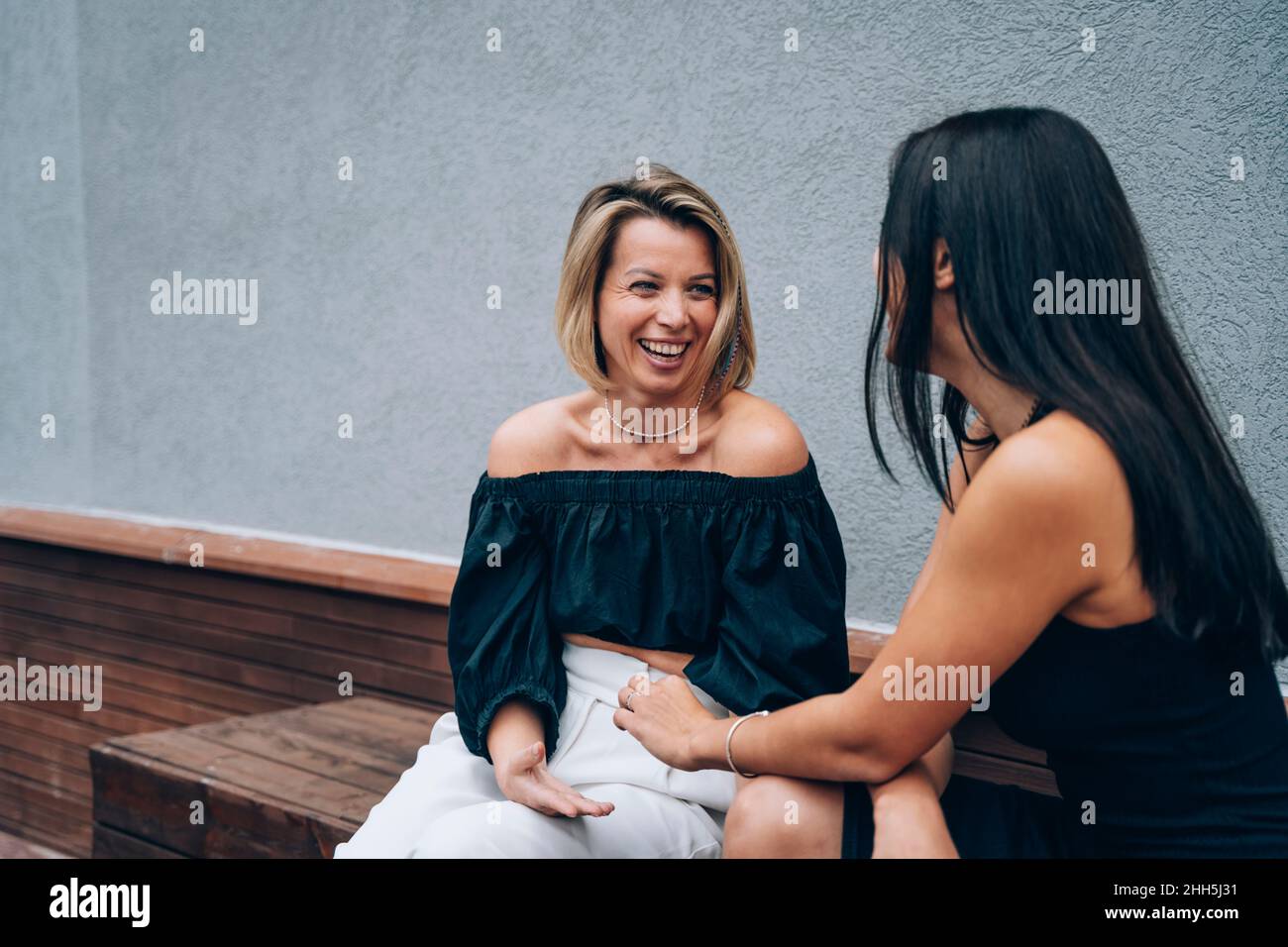 Cheerful friends talking to each other sitting on bench Stock Photo - Alamy