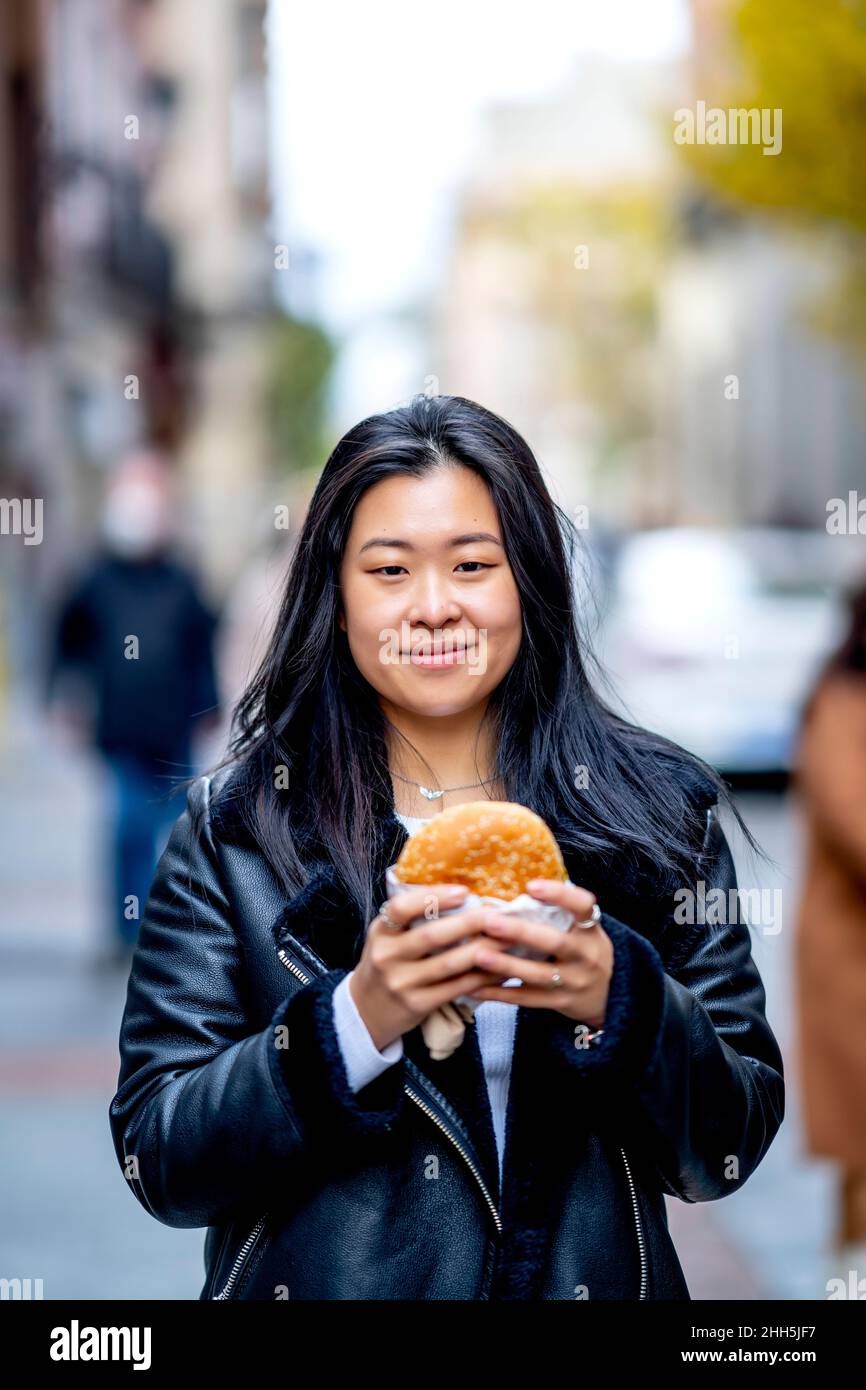 Smiling young woman with long black hair holding burger Stock Photo - Alamy