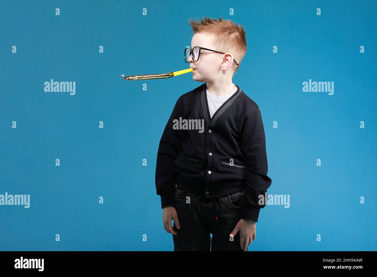 Cheerful little child boy 7s years old in glasses blowing festive pipe ...