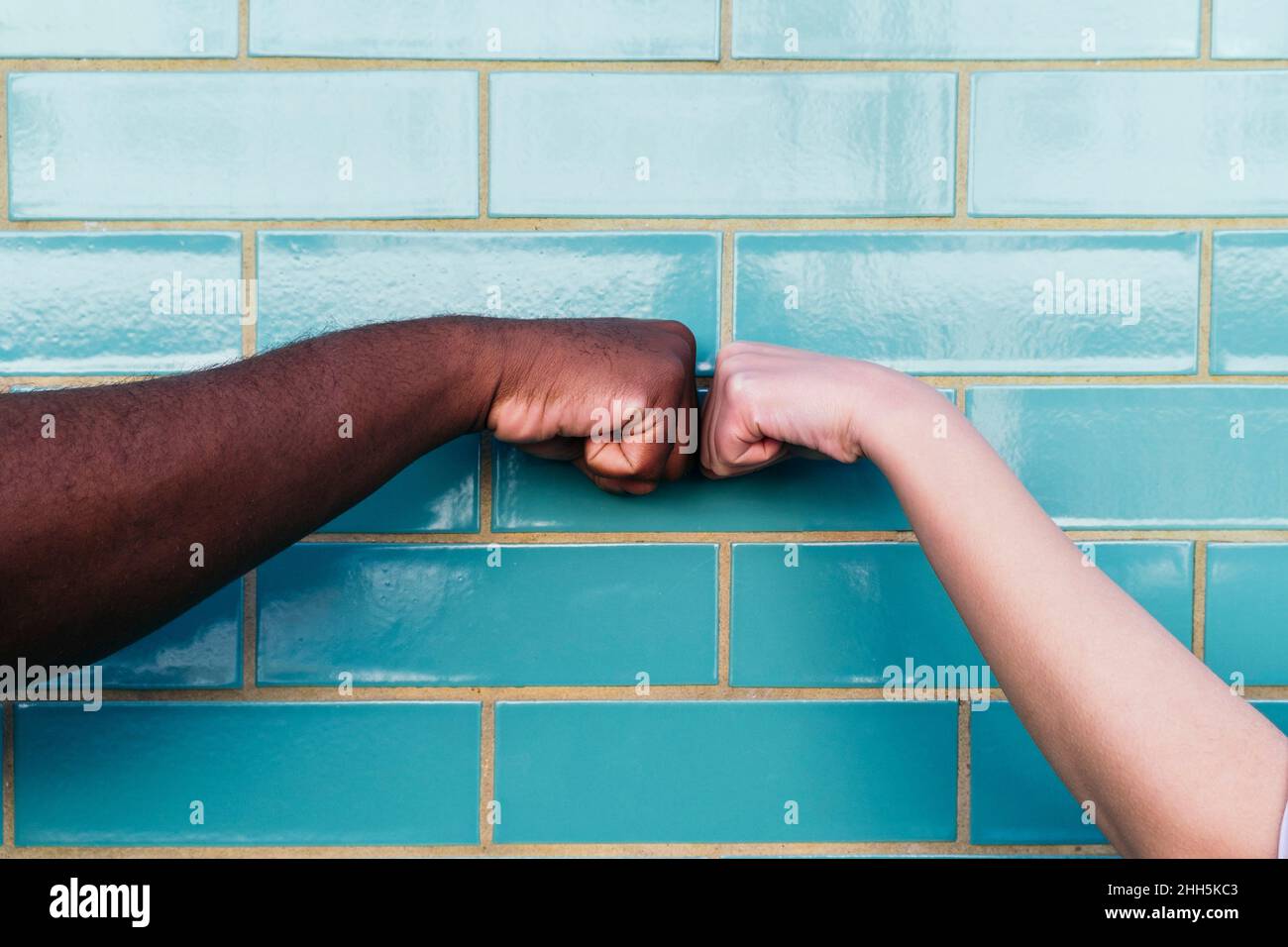 Man and woman giving fist bump on turquoise brick wall Stock Photo - Alamy