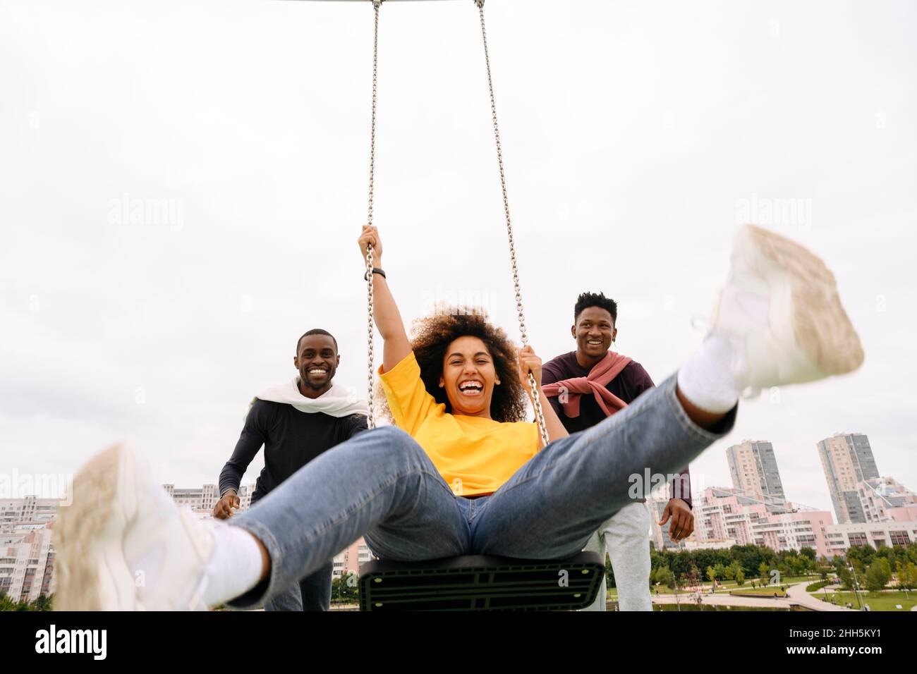 Happy men pushing friend sitting on swing in park Stock Photo - Alamy