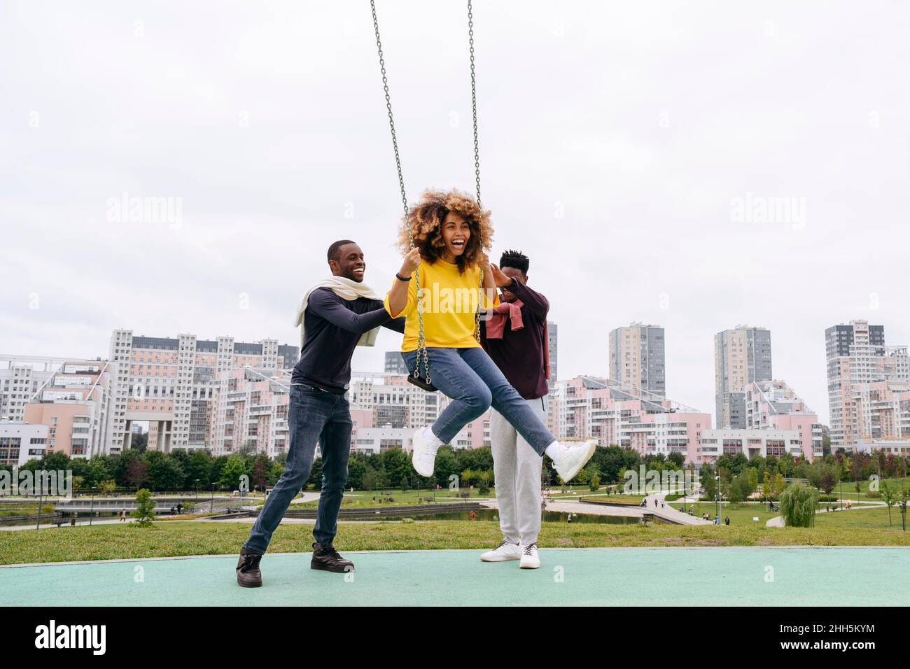 Men pushing friend on swing in front of sky Stock Photo - Alamy