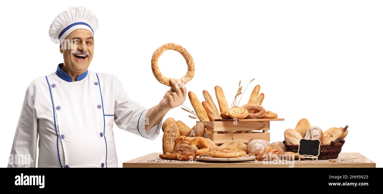 Mature male baker holding a baked pastry next to a table with different ...