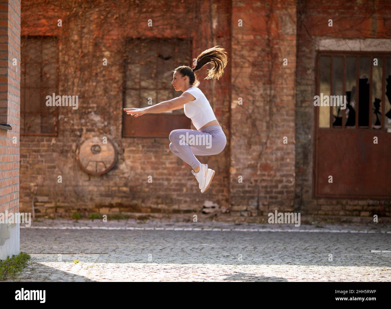 Pretty young woman juping high during training in the urban environment ...