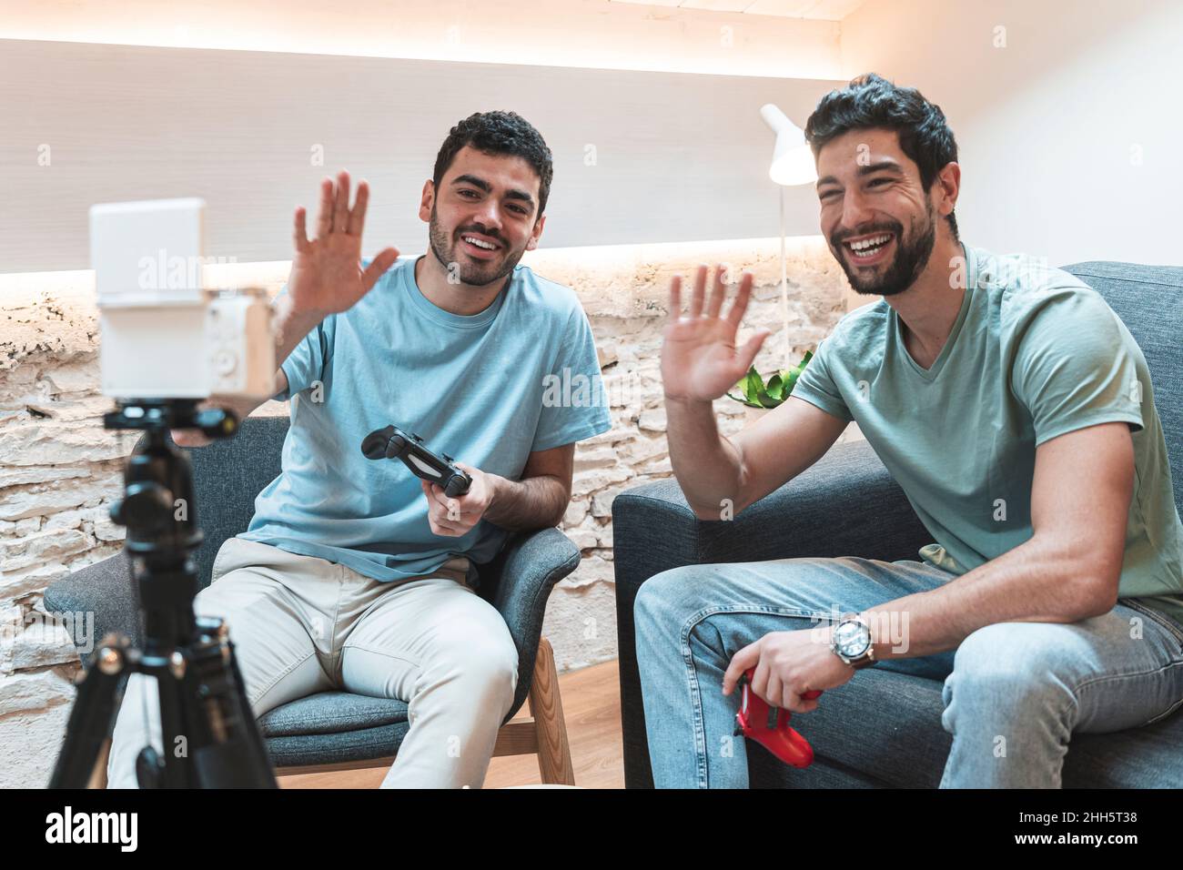 Smiling friends with video game controllers waving at camera on tripod ...