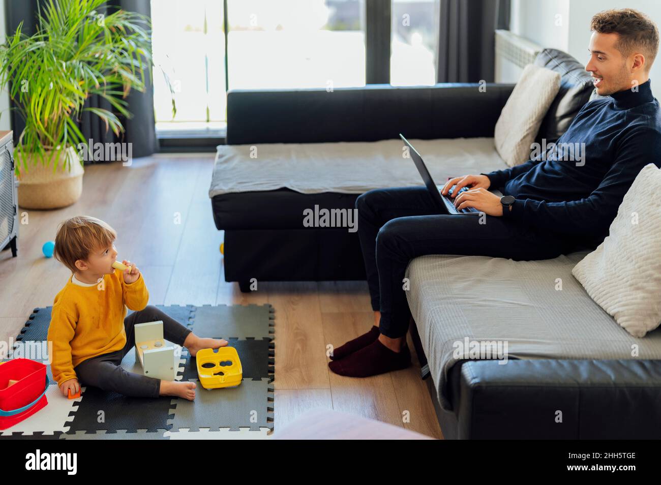 Baby boy looking at father working on laptop in living room Stock Photo ...