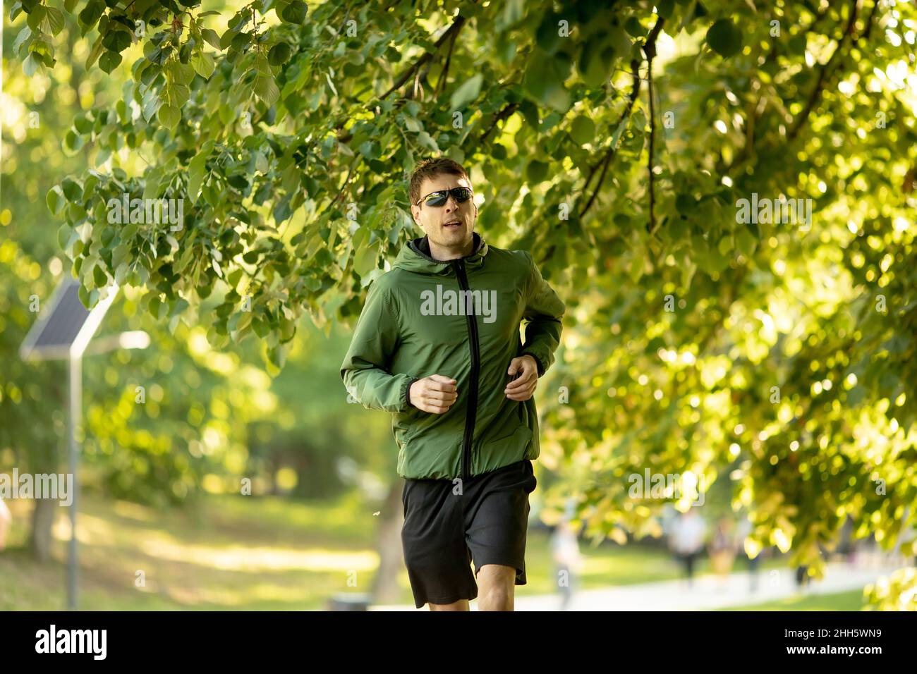 Handsome athletic young man running while doing workout in sunny green ...