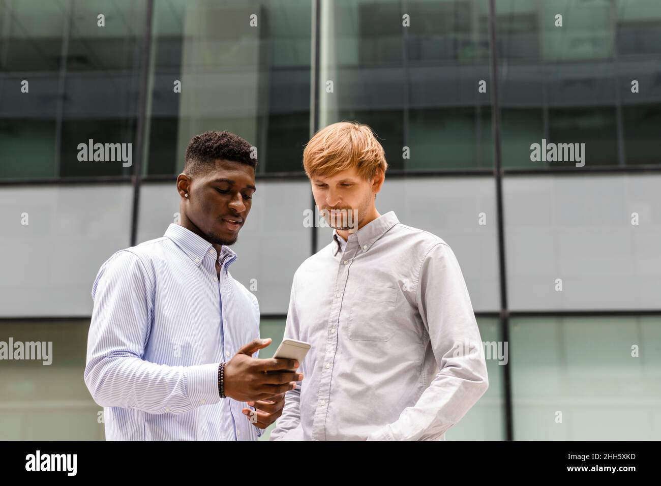 Man sharing mobile phone with friend in front of building Stock Photo ...