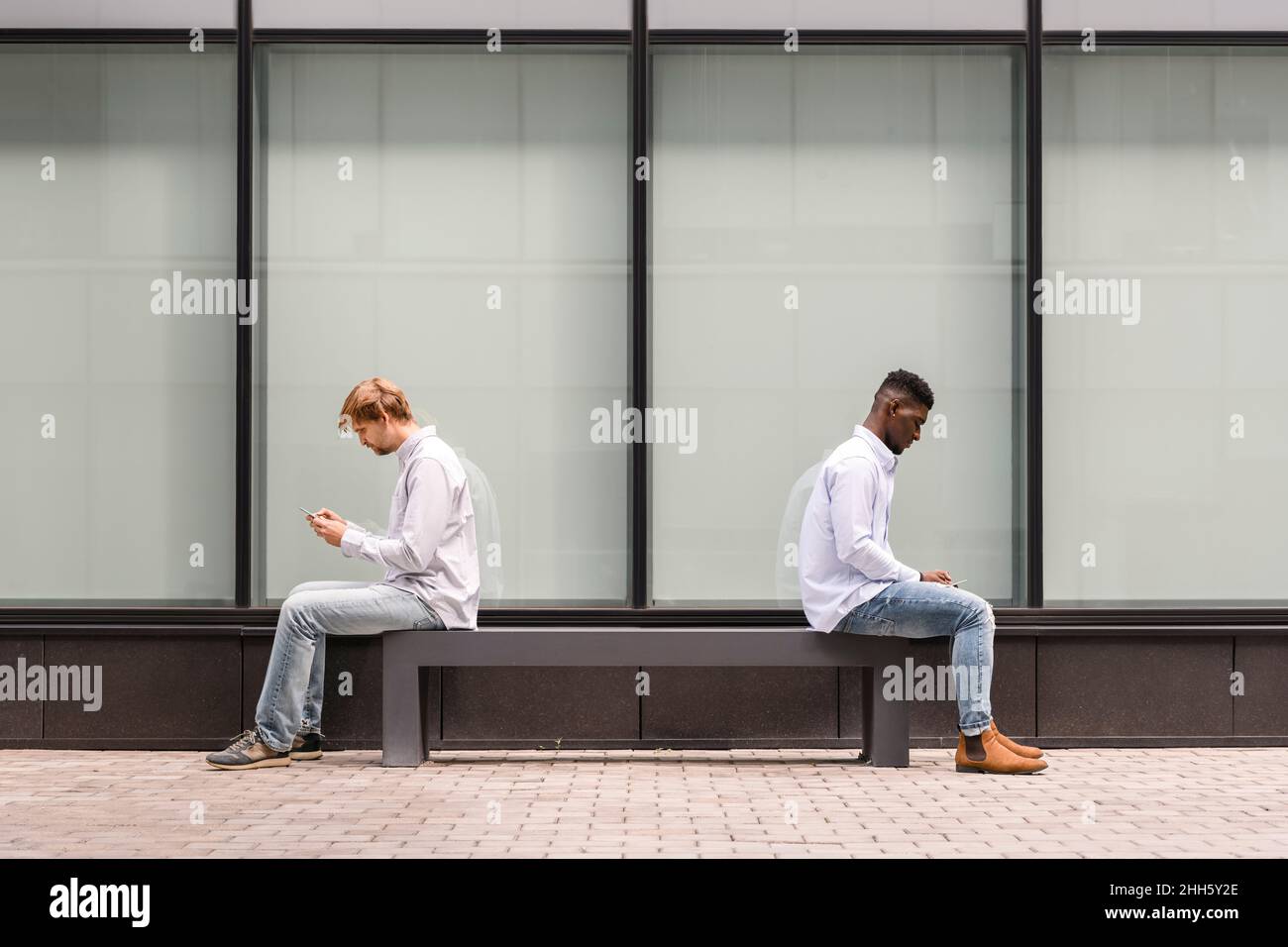 Friends sitting back to back using smart phone on bench Stock Photo - Alamy