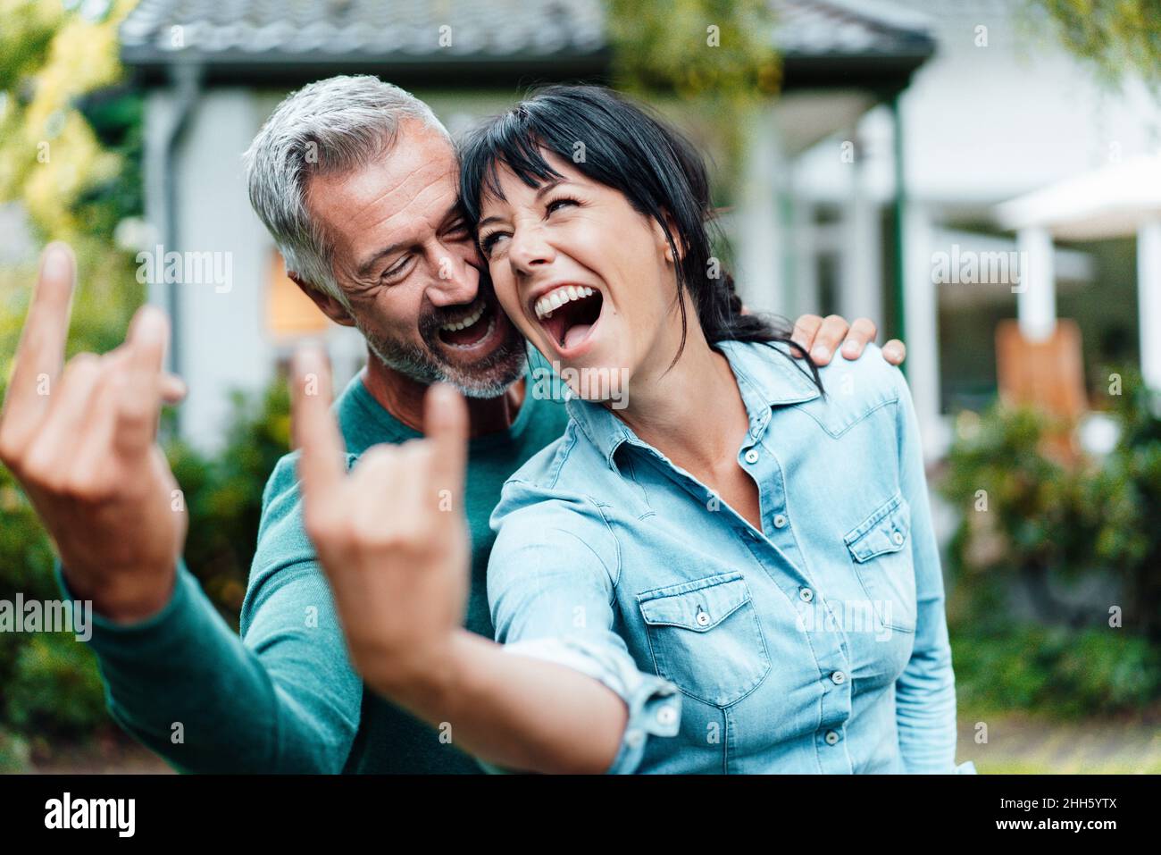 Cheerful making couple gesturing horn sign in backyard Stock Photo - Alamy