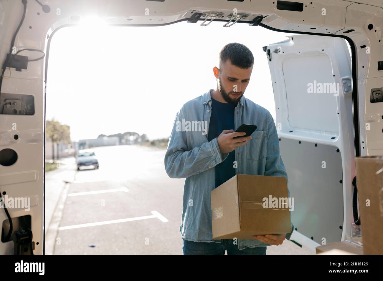 Delivery man using mobile phone holding box at van doorway Stock Photo ...