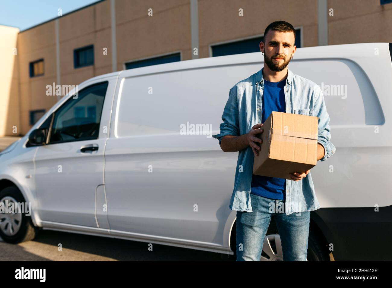 Young delivery man with package standing in front of van Stock Photo ...