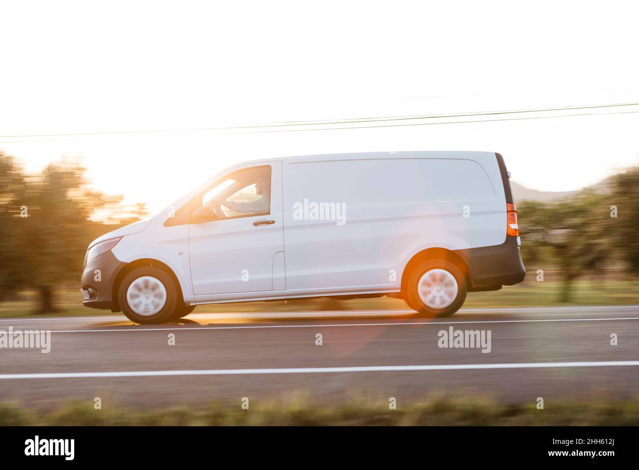 Delivery man driving van on road at sunset Stock Photo - Alamy