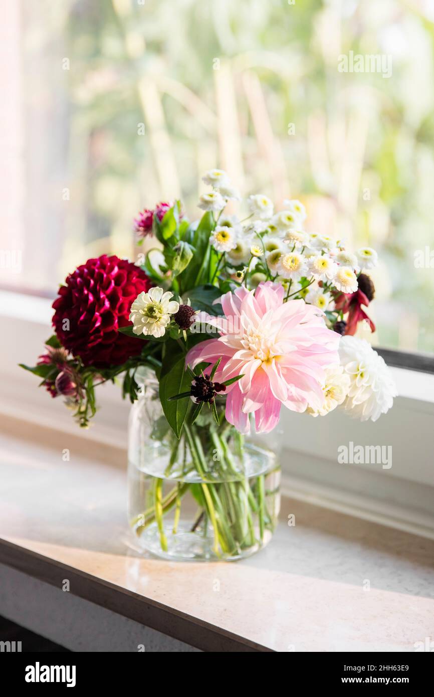 Jar with colorful flowers standing on window sill Stock Photo - Alamy