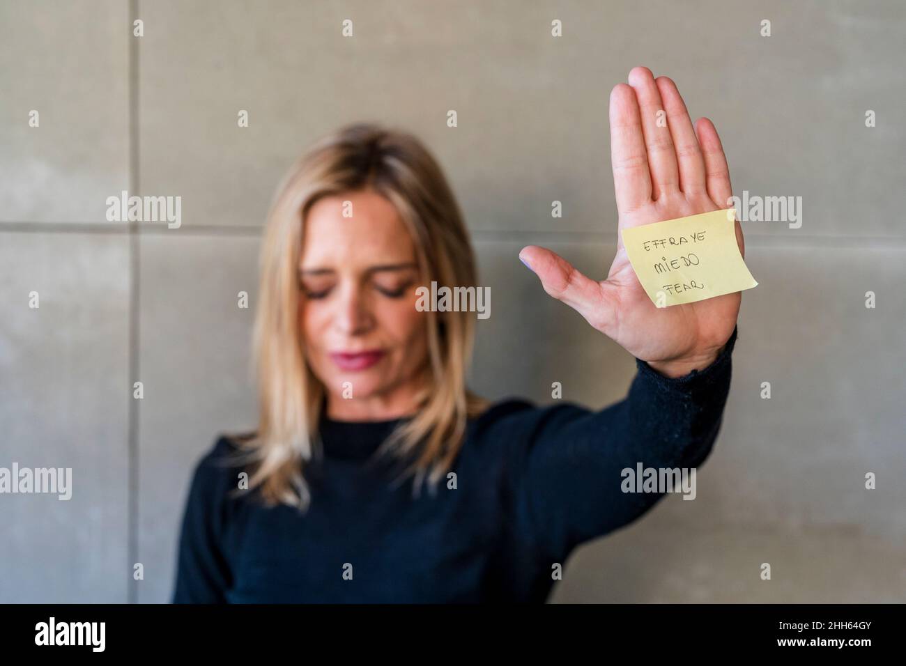 Scared blond woman showing text fear written on sticky note in front of ...