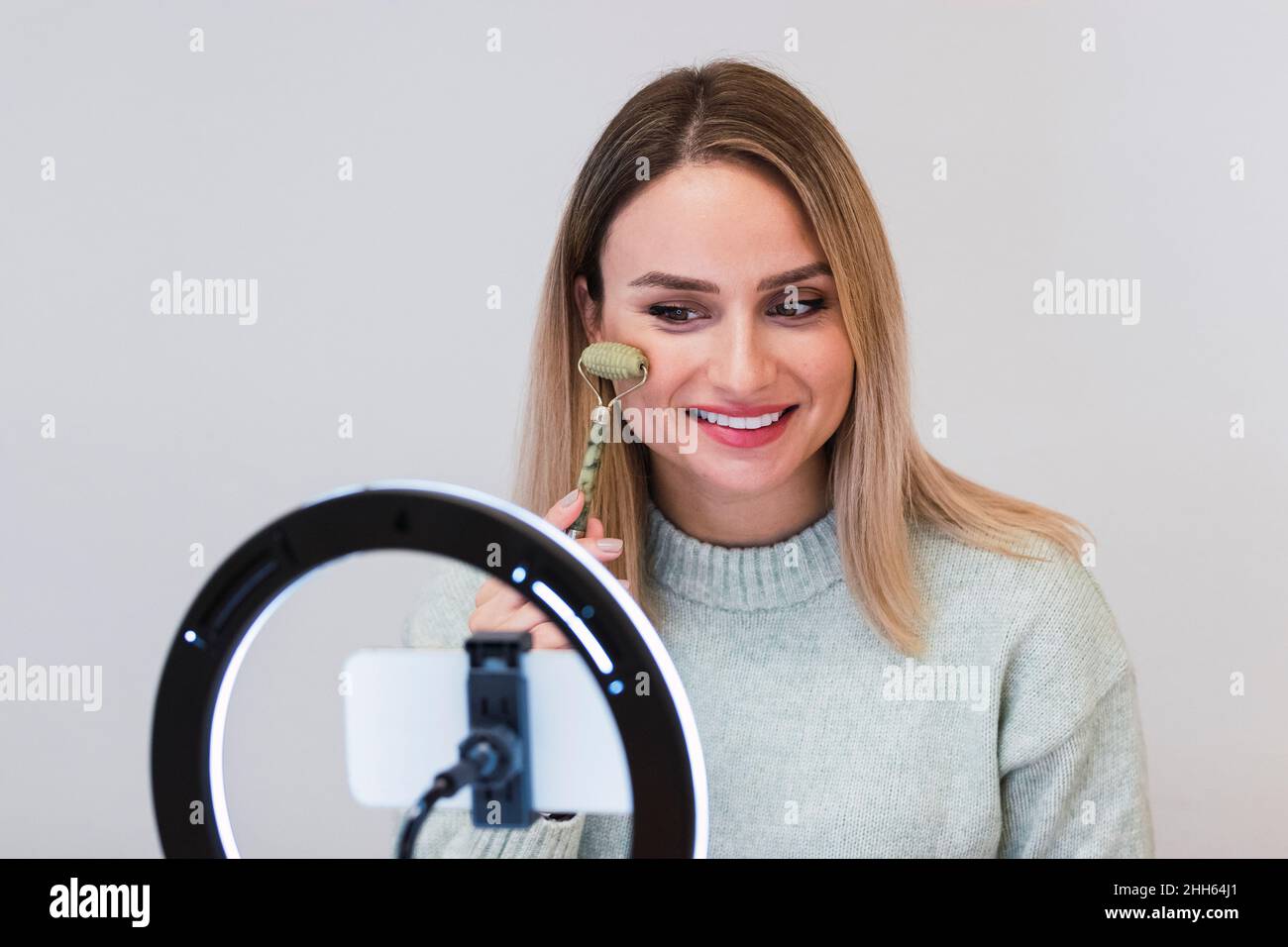 Smiling influencer filming tutorial with jade roller in front of ring ...