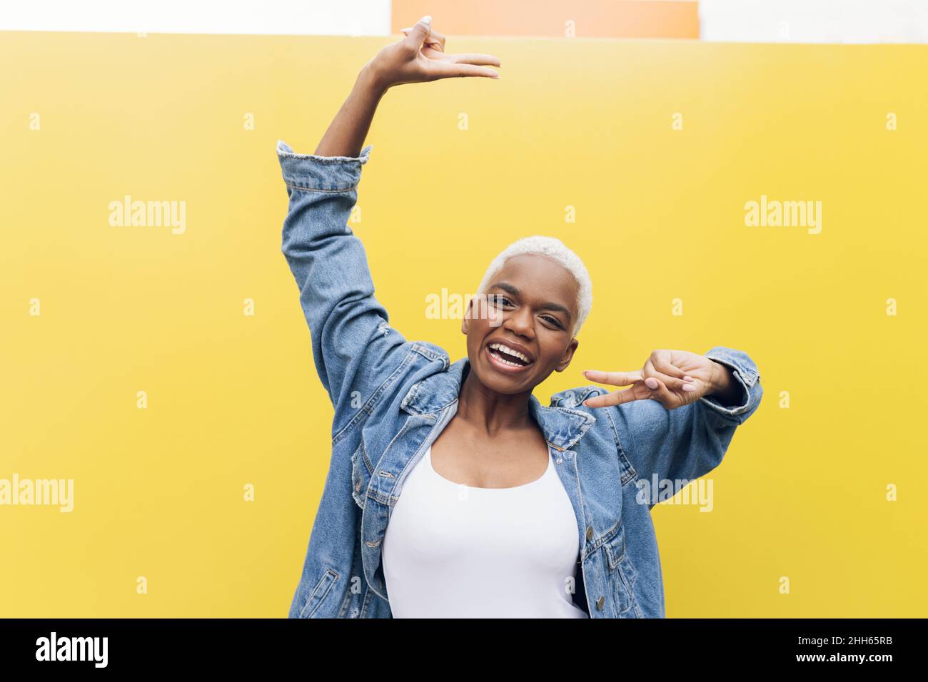 Happy woman making peace sign gesture against yellow background Stock ...
